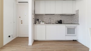 Uma cozinha compacta com armários brancos, painel de azulejos, forno embutido e piso de madeira.