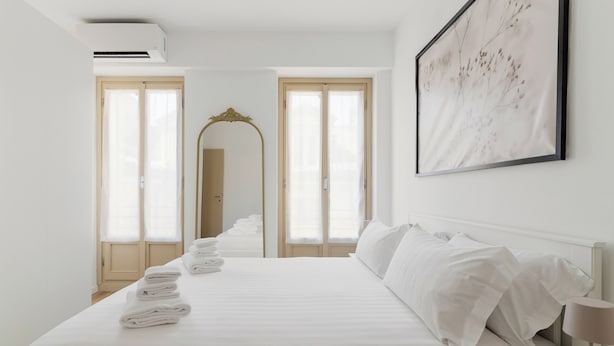 Quarto de hotel com uma cama bem arrumada, um espelho grande e uma obra de arte emoldurada na parede.