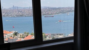 Quarto com grande janela dando vista para a paisagem urbana e um corpo d'água.