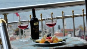Mesa com garrafa de vinho, dois copos e prato de frutas em varanda com vista para a cidade.