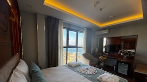 Quarto de hotel com uma cama grande, uma mesa de trabalho com televisão, vista para a cidade e varanda.