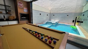 Uma mesa de bilhar com bolas, uma mesa de bilhar e uma pequena mesa de bilhar numa sala com vista para uma piscina.