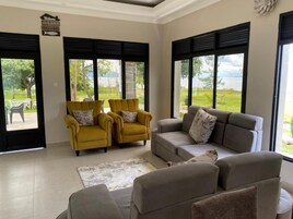 Uma sala de estar com dois poltronas amarelas, um sofá cinza e vista para um lago.