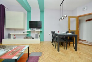 Uma sala de estar moderna com televisão de tela plana, uma mesa de jantar com cadeiras e uma cozinha com geladeira e micro-ondas.