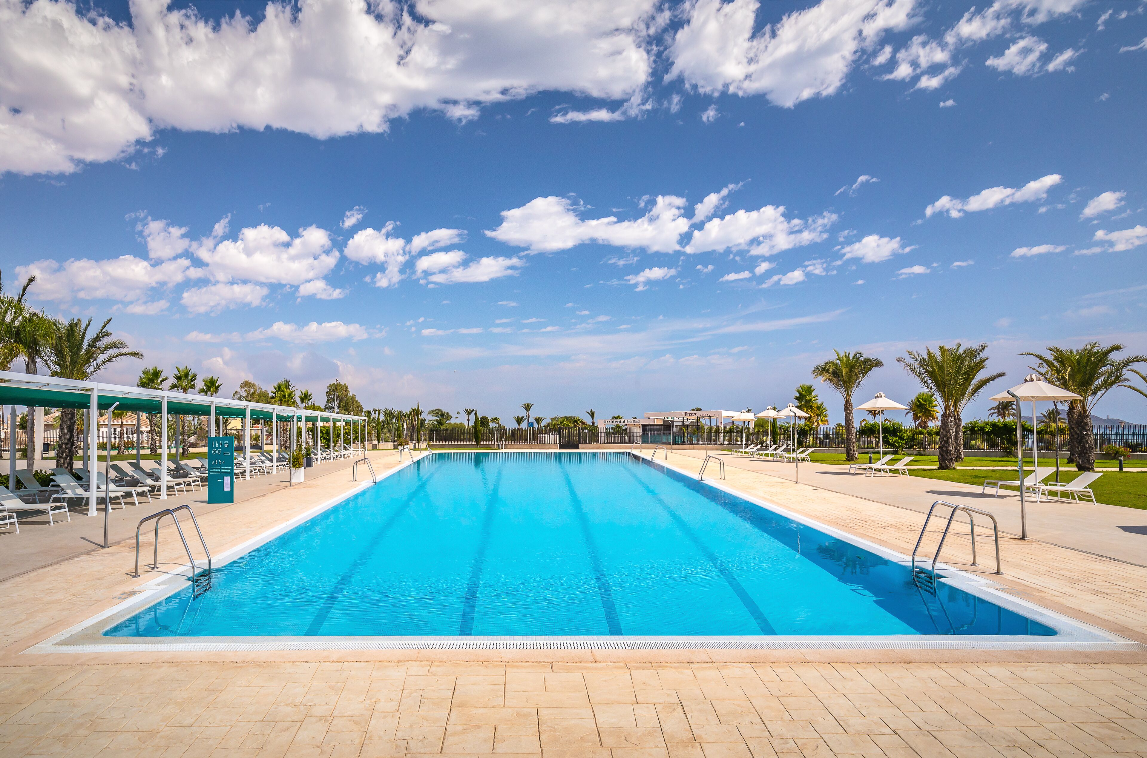Piscina retangular com água azul cristalina, ladeada por um deck revestido e espreguiçadeiras.