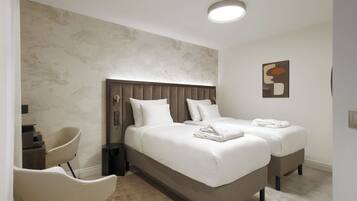 Quarto de hotel moderno com uma cama grande, duas mesas de cabeceira, uma cadeira e uma pequena escrivaninha.