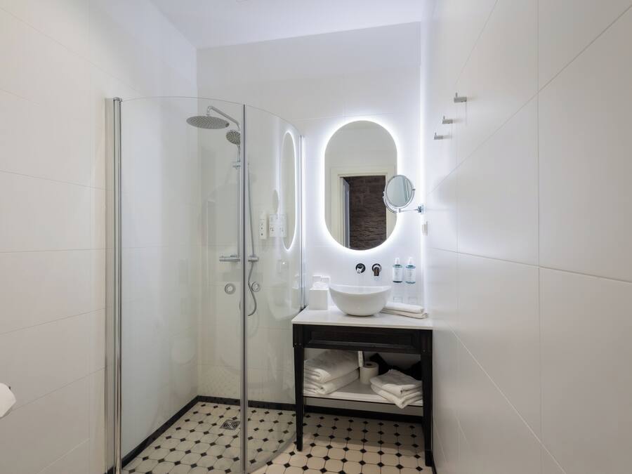 Uma casa de banho moderna com cabine de duche em vidro, lavatório branco, espelho redondo e chão em mosaico preto e branco.
