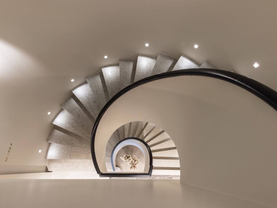Escadaria espiral moderna com design minimalista, destacando corrimão curvo e iluminação embutida.