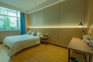 Quarto de hotel com cama, mesa de cabeceira, abajur e vista para o verde lá fora.