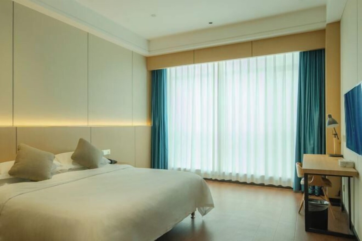Quarto de hotel com uma cama grande, uma escrivaninha e uma televisão.