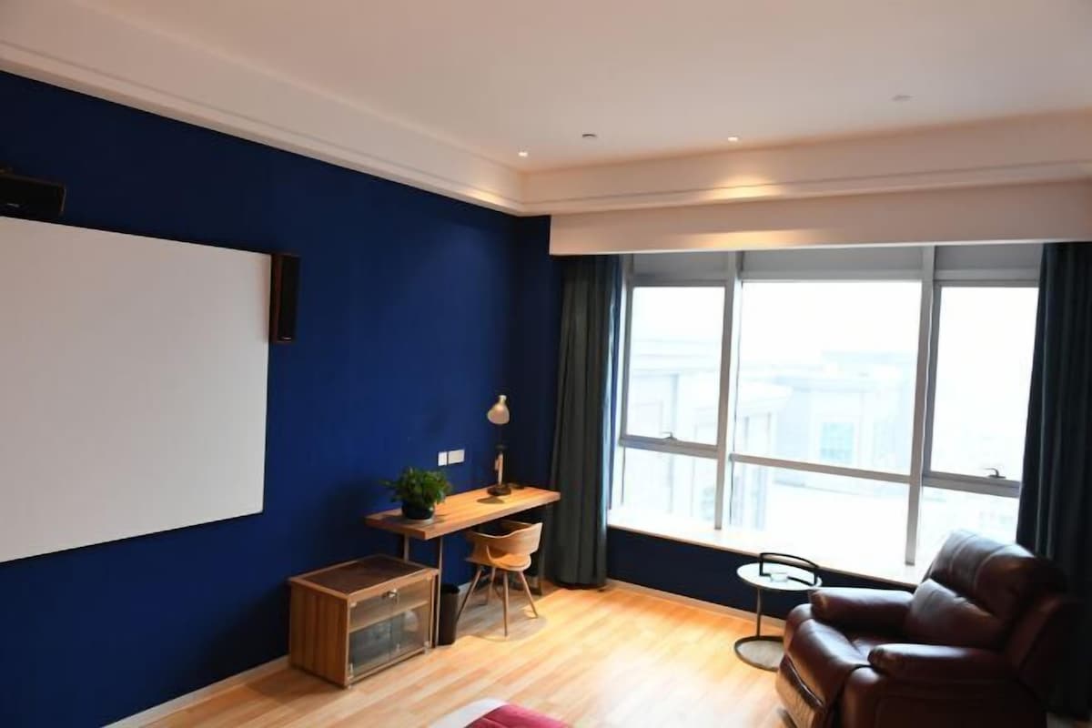 Uma sala de estar moderna com uma janela grande, uma escrivaninha, um sofá de couro e uma mesinha.