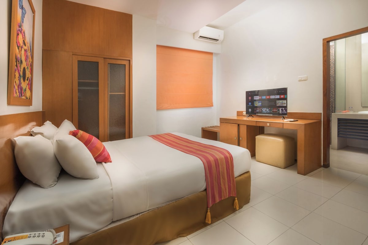 Quarto de hotel com cama, escrivaninha, televisão e banheiro.