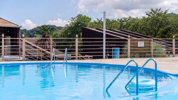 Piscina com escada de metal, espreguiçadeiras e área de deck de madeira.
