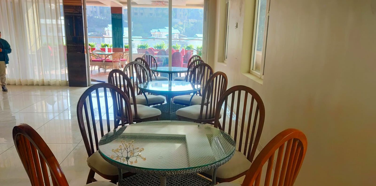 Uma sala de jantar com mesas e cadeiras redondas, janelas amplas e vista para o exterior.