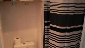 Casa de banho pequena e compacta, com sanita, uma prateleira sobre a sanita e uma cortina de chuveiro riscada.