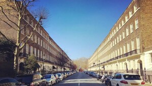 Rua com carros estacionados e edifícios com várias janelas e varandas.