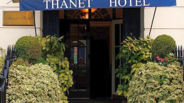 A entrada do Hotel Thanet, com uma marquise azul, uma placa e plantas em vasos.