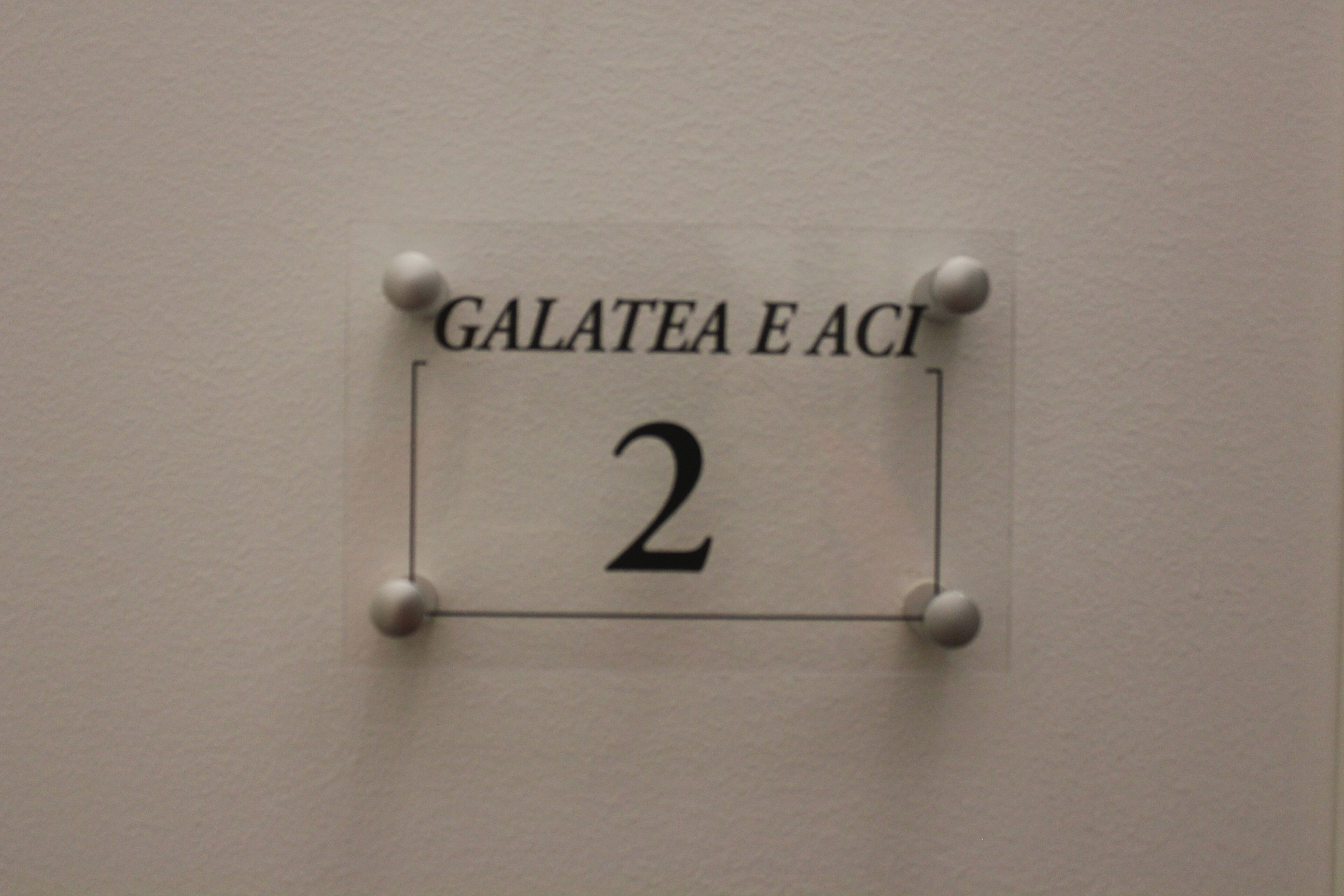 Um letreiro fixado na parede com o texto 'GALATEA E ACI' e o número '2'.