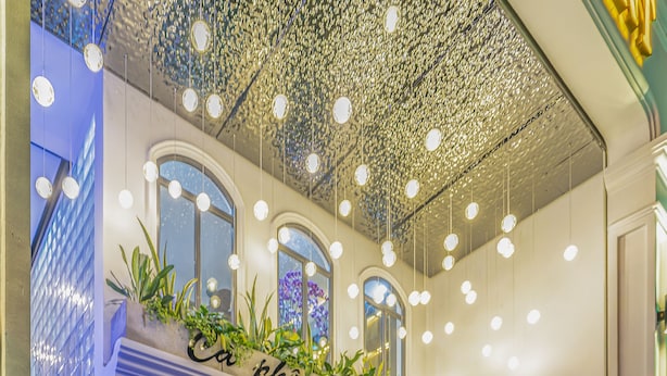 Um hall de hotel moderno com uma cafeteria, escadaria e plantas em vasos.