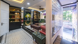 Um interior moderno com piso estampado, área de estar com sofá e puf, e uma estante com objetos decorativos.