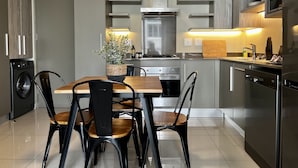 Uma cozinha moderna com eletrodomésticos embutidos, um espaço de refeições com mesa e cadeiras de madeira, e uma janela grande que oferece muita luz natural.