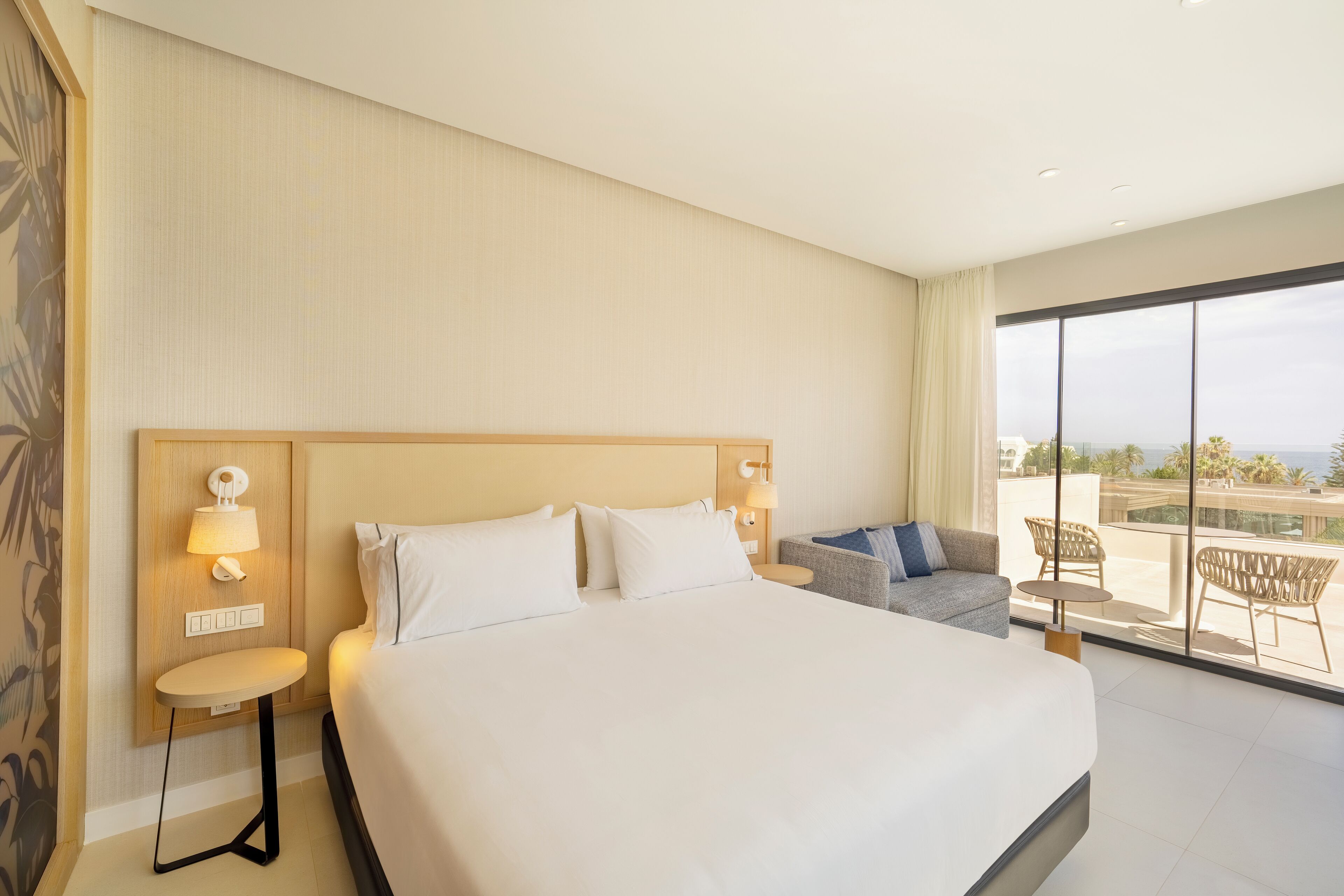 Quarto de hotel com uma cama grande, um sofá pequeno, uma mesa e uma varanda com cadeiras.