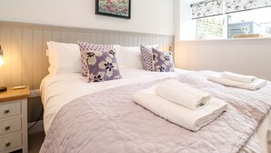 Uma cama bem arrumada com cabeceira acolchoada, duas almofadas decorativas e uma toalha dobrada sobre a cama.