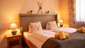 Quarto de hotel com duas camas, mesa de cabeceira com abajur, almofadas decorativas, cabeceira e janela com cortinas.