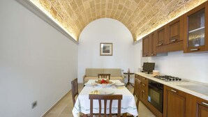 Uma sala de jantar com uma mesa posta para dois, um sofá e uma cozinha com armários de madeira e fogão a gás.