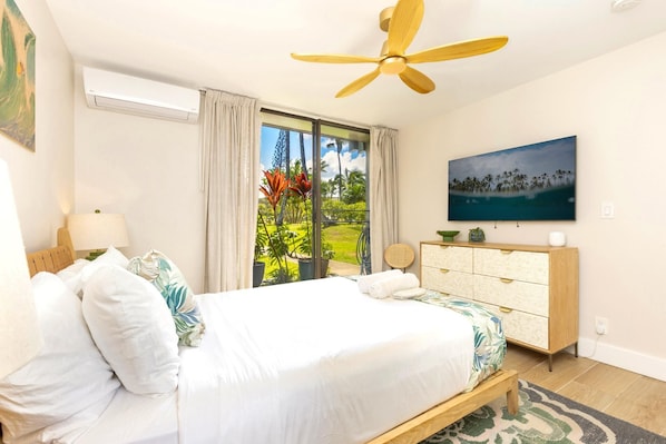 Quarto com cama, ventilador de teto, televisão, cômoda e vista para um jardim por uma porta de correr.