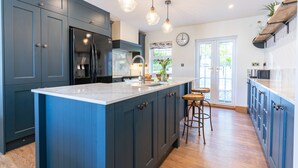 Uma cozinha moderna com armários azul escuro, uma ilha grande, eletrodomésticos de aço inoxidável e iluminação pendente.