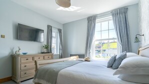 Quarto com cama, cômoda, televisão e janelas amplas.