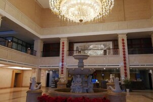 Um hall espaçoso com um lustre imponente, uma fonte central e uma varanda com decoração vermelha.