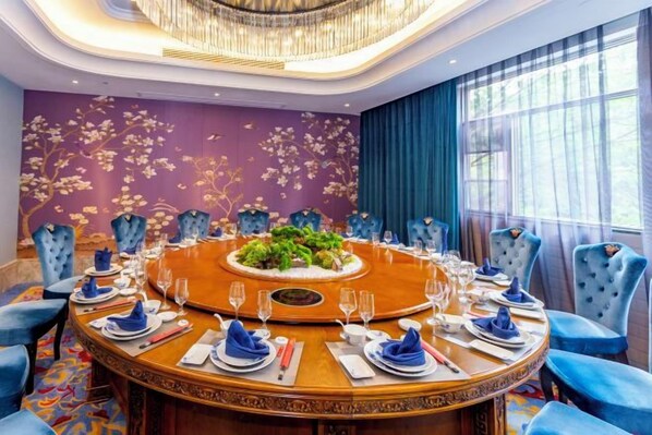 Sala de conferência com mesa redonda, cadeiras estofadas azuis e design floral na parede.