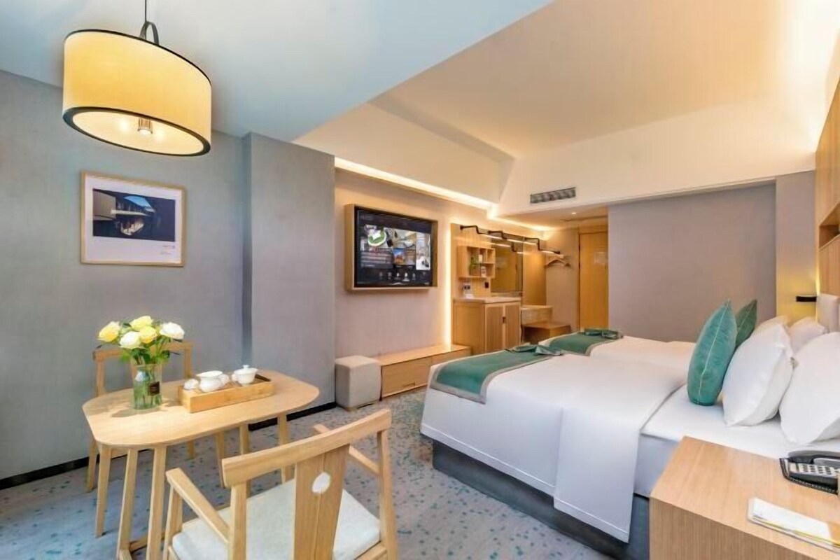 Quarto de hotel com cama, escrivaninha, cadeira, televisão e banheiro.