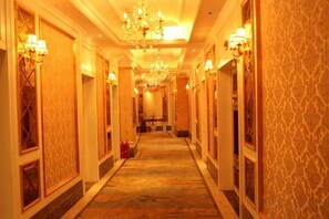 Corredor de hotel com lustres, papel de parede estampado e piso coberto por carpete.