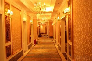 Corredor de hotel com lustres, papel de parede estampado e piso coberto por carpete.