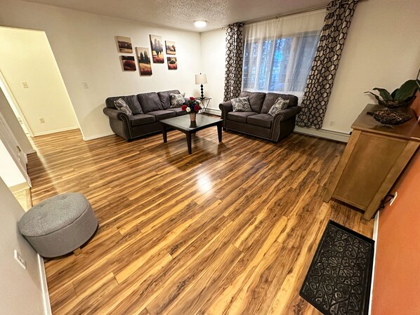 Uma sala de estar com dois sofás, uma mesa de centro, um banquinho cinza e um armário.