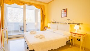 Quarto de hotel com uma cama, duas mesas de cabeceira com abajures, uma janela com cortinas amarelas e um quadro na parede.
