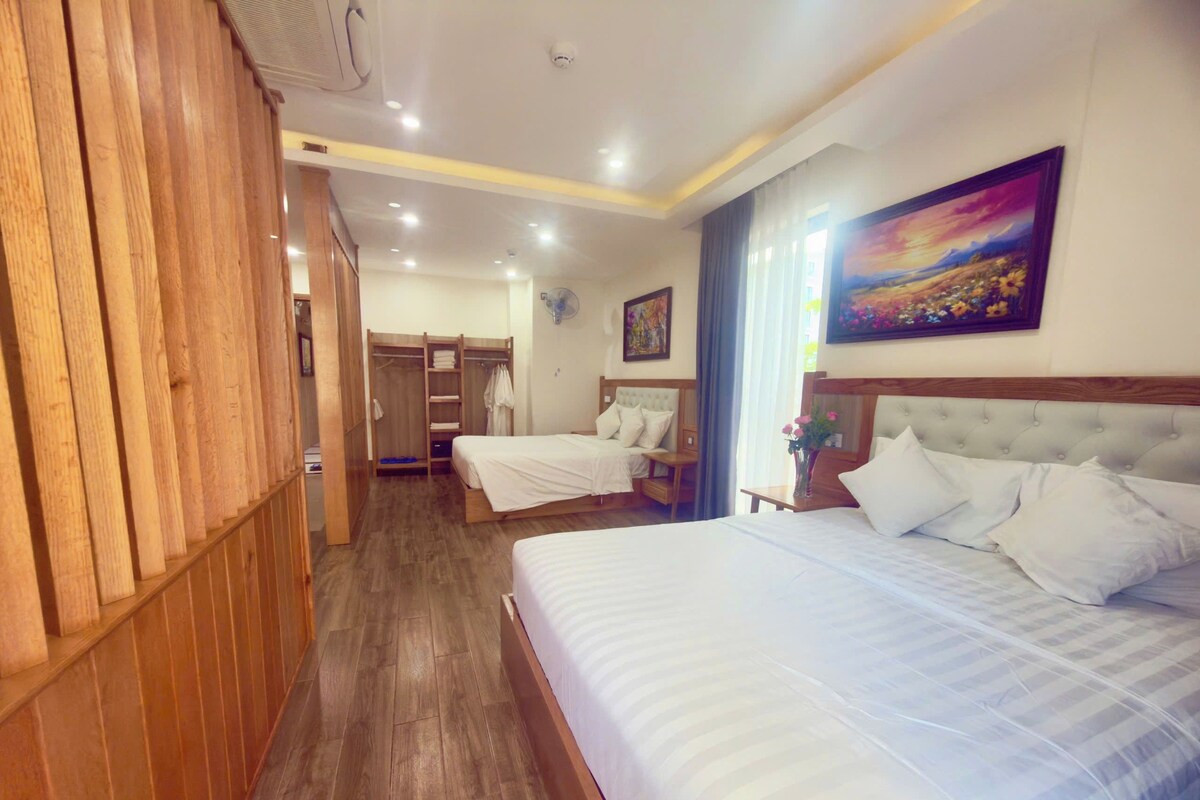Quarto de hotel com duas camas, piso de madeira, ventilador de teto e um quadro na parede.