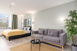 Quarto moderno com uma cama, um sofá cinza, uma mesinha com um vaso e uma planta em vaso.