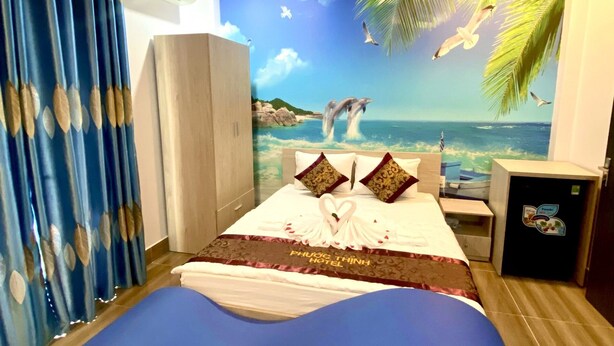 Quarto de hotel com cama, pequena escrivaninha, minibar e um mural com cena de praia.