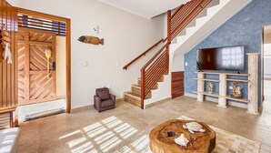 Uma sala de estar com escada de madeira, televisão em uma estante e um peixe decorativo na parede.