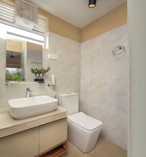 Casa de banho moderna com lavatório branco, sanita e paredes de mármore.