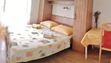 Quarto com cama, mesa de cabeceira, cadeira e uma pequena mesa com um vaso.