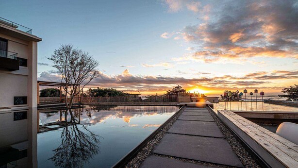 Um edifício moderno com piscina no terraço refletindo o pôr do sol.
