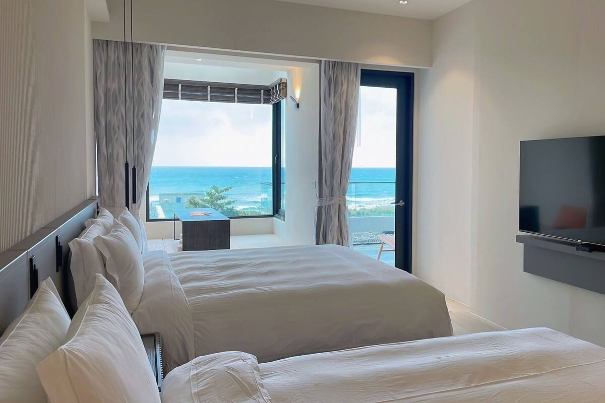 Quarto de hotel com duas camas, televisão e vista para o oceano.