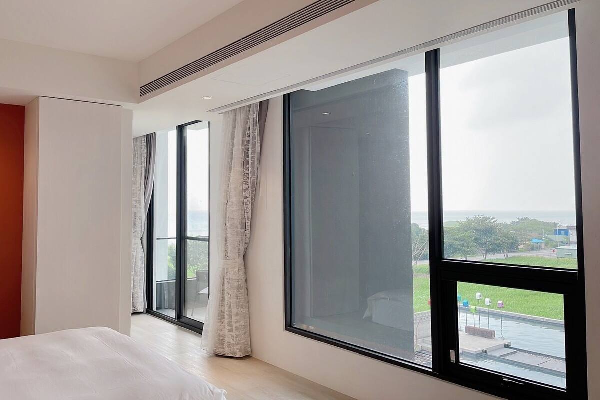 Quarto de hotel moderno com uma janela grande, uma cama e vista para o exterior.