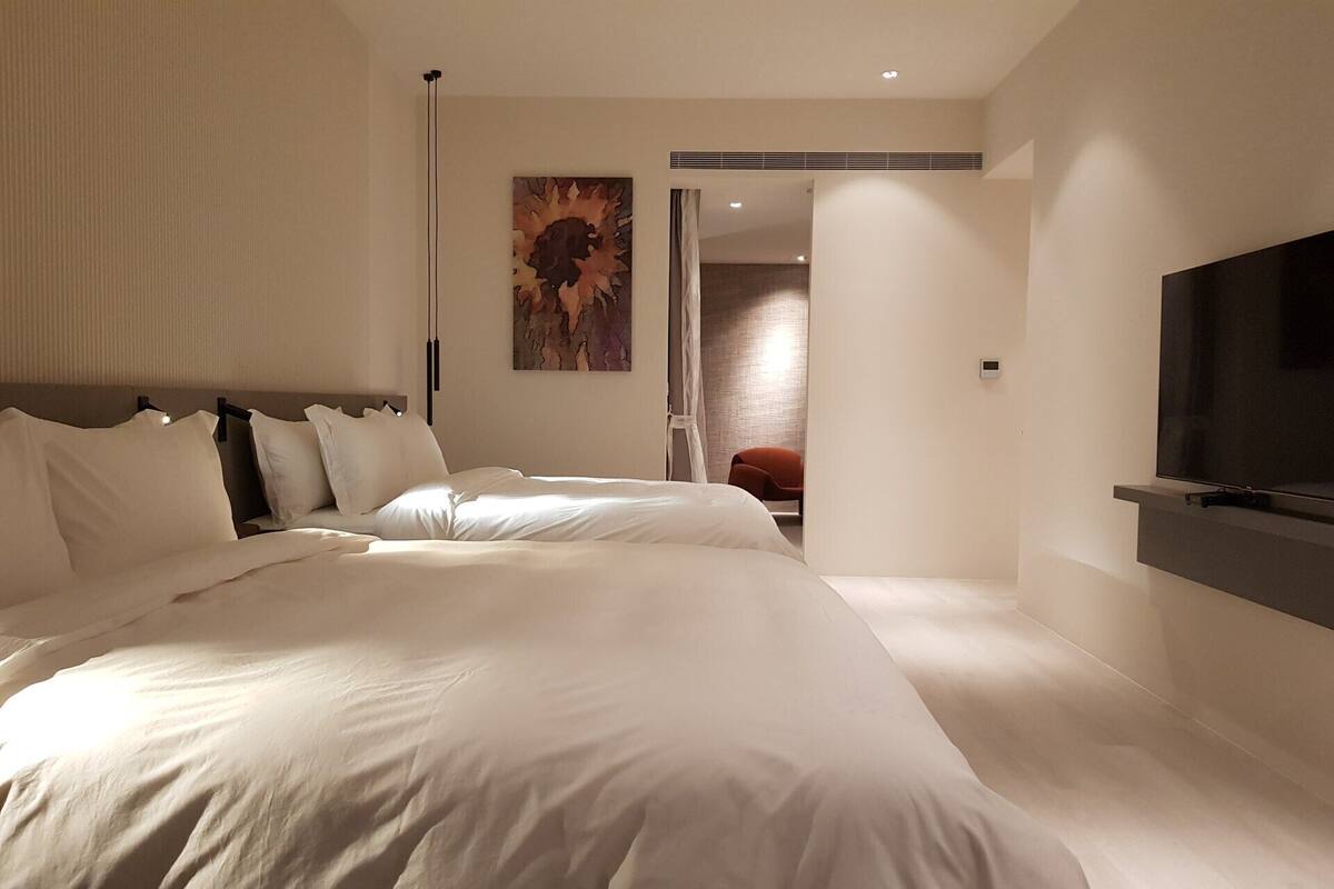 Quarto de hotel moderno com duas camas, uma televisão de tela plana e um quadro grande na parede.
