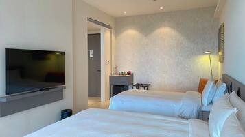 Quarto de hotel com duas camas, televisão, escrivaninha com cadeira e uma pequena mesa.
